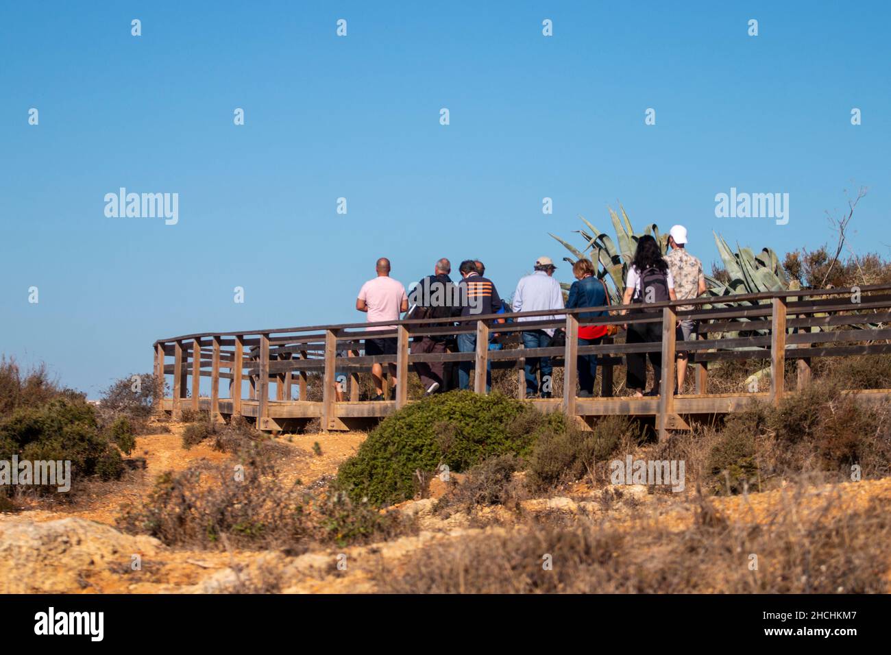Tourists walking by on wooden boardwalk near the coastline cliffs of ...