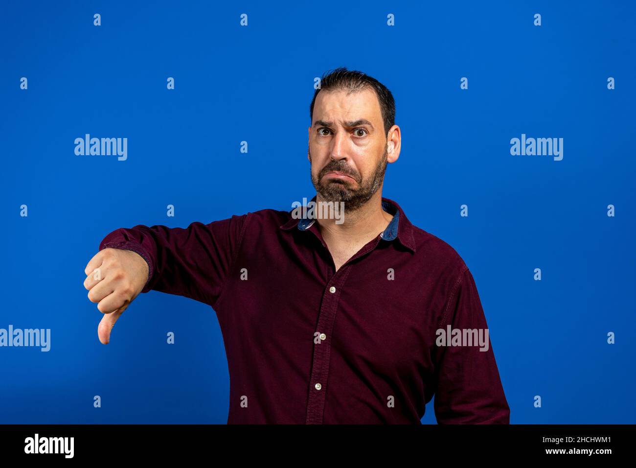 Young casual man making the thumbs down negative hand sign on blue ...