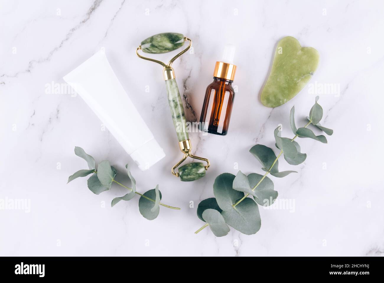 Flat lay with jade facial roller and gua sha tool with beauty serum ...