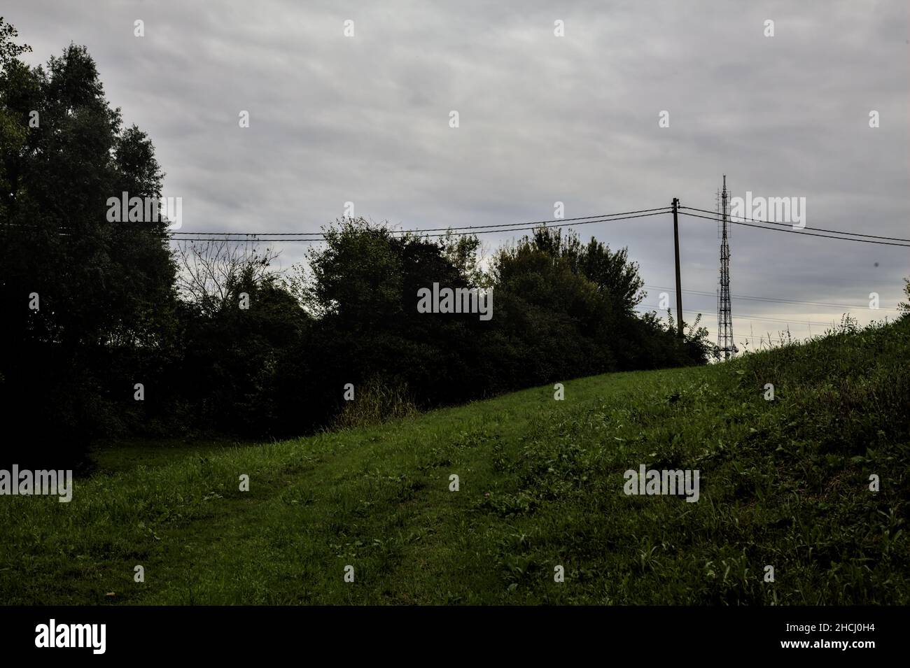 Grassy path on a slope in a field with over head cables on a cloudy day ...