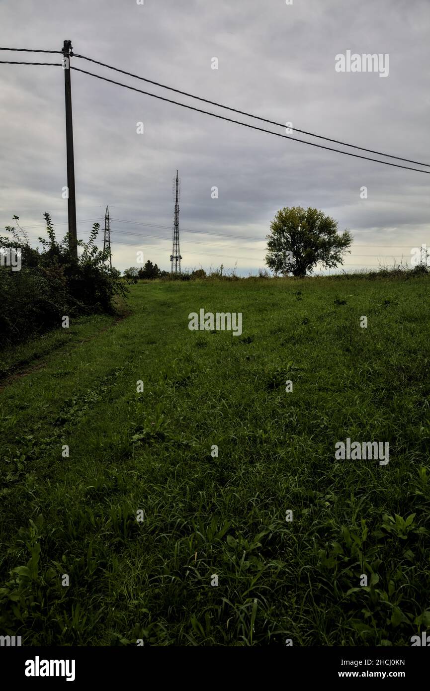 Grassy path on a slope in a field with over head cables on a cloudy day ...