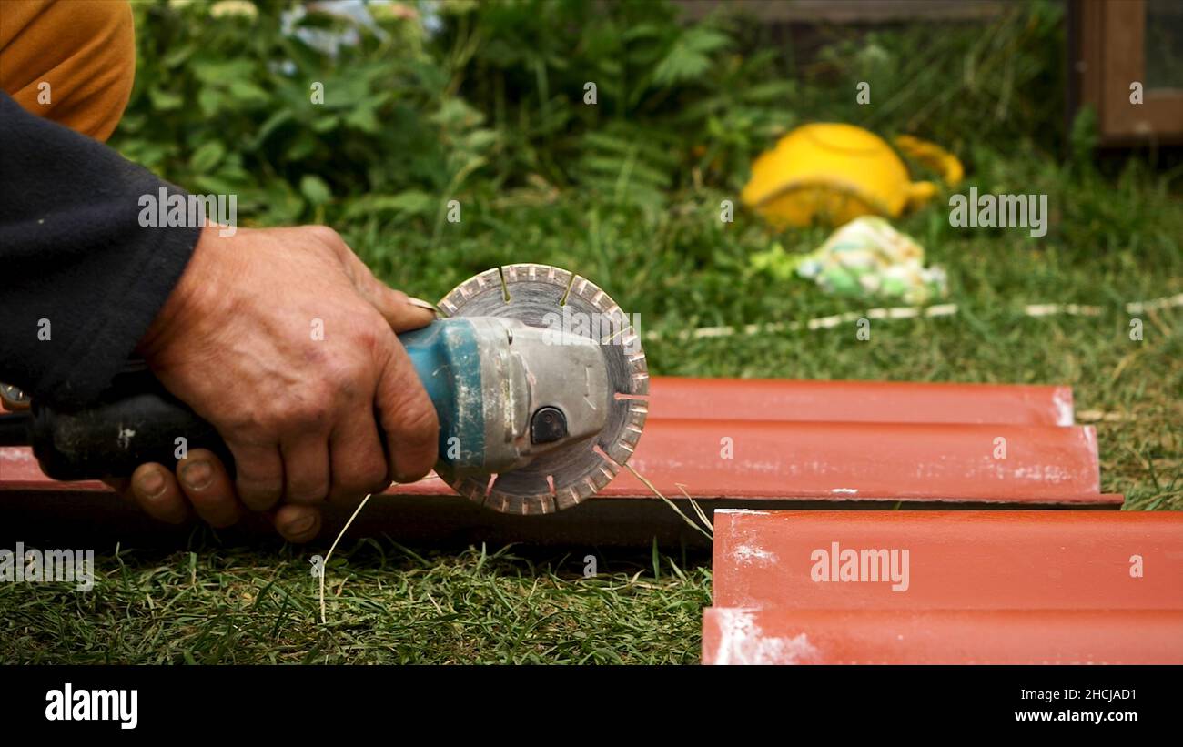 Roofer using an angle grinder machine to cut a roof tile of red color ...