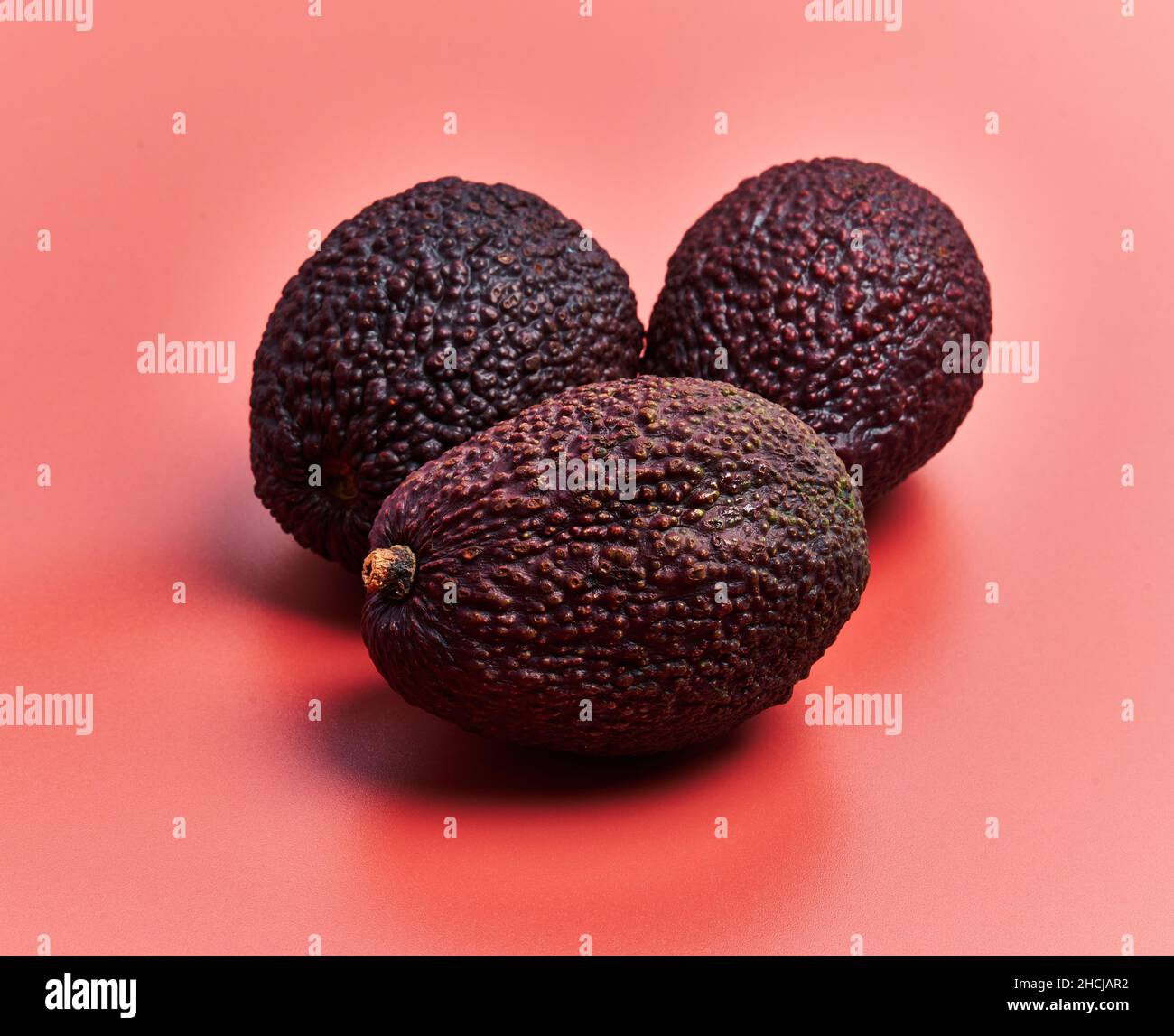 Three avocados fruit over red background Stock Photo - Alamy