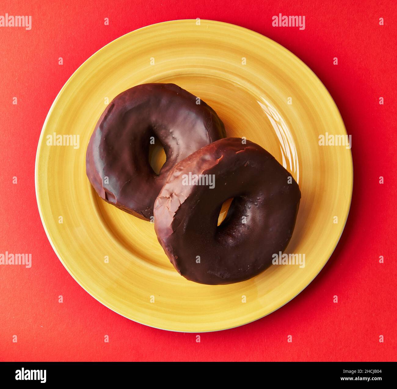 Plate of two chocolate doughnuts on a red background Stock Photo - Alamy