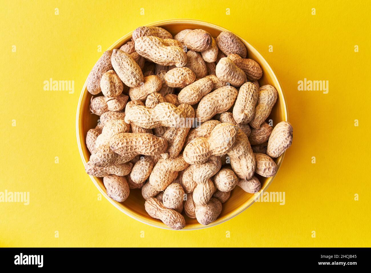 Bowl of peanuts with shell on a yellow background Stock Photo - Alamy