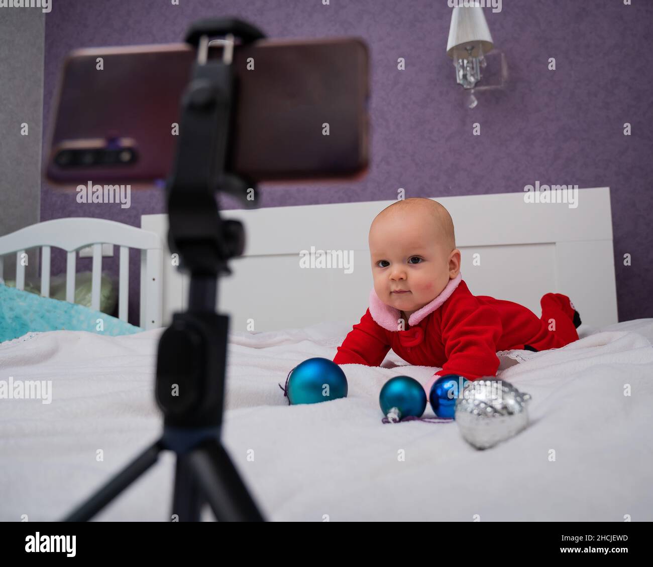 A baby boy dressed in a Santa suit sits on the bed and looks at the ...