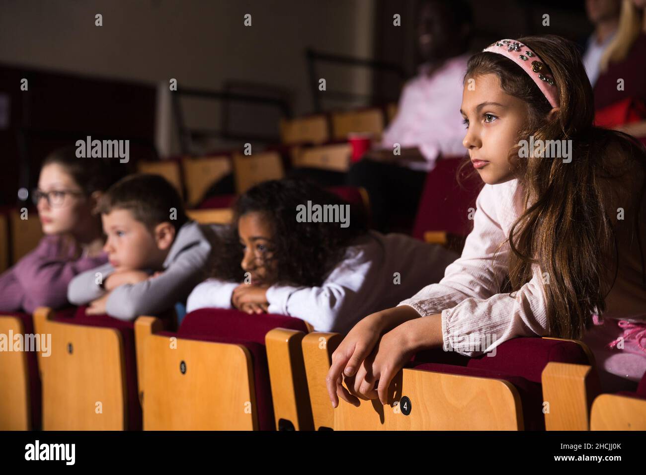 Preteen girl with other children absorbedly watching movie in cinema ...
