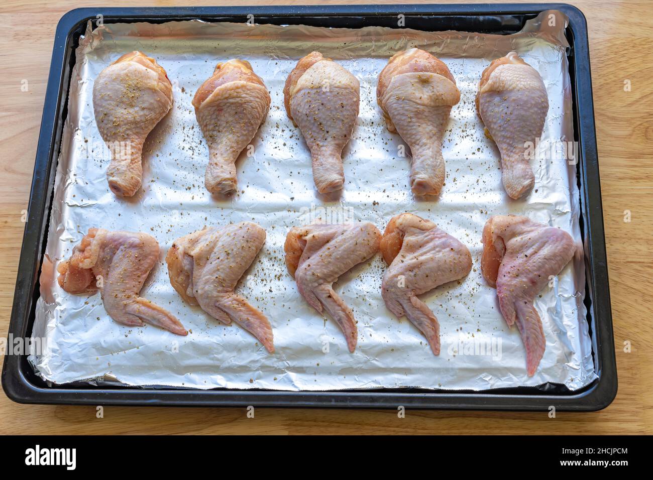 Raw chicken legs and wings lined in a row on aluminium foil background ...
