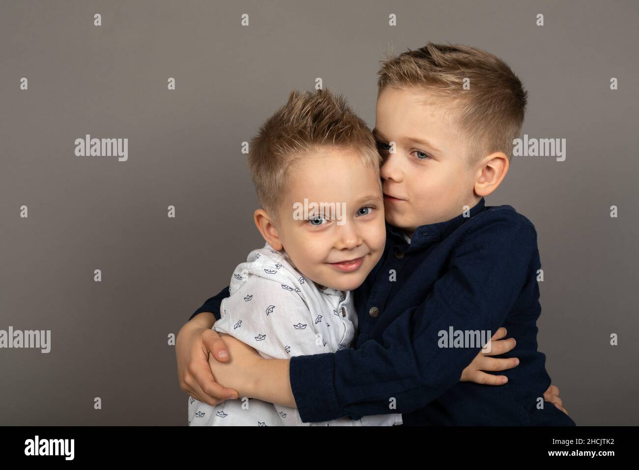 Two brothers hugging each other in front of a grey background Stock ...