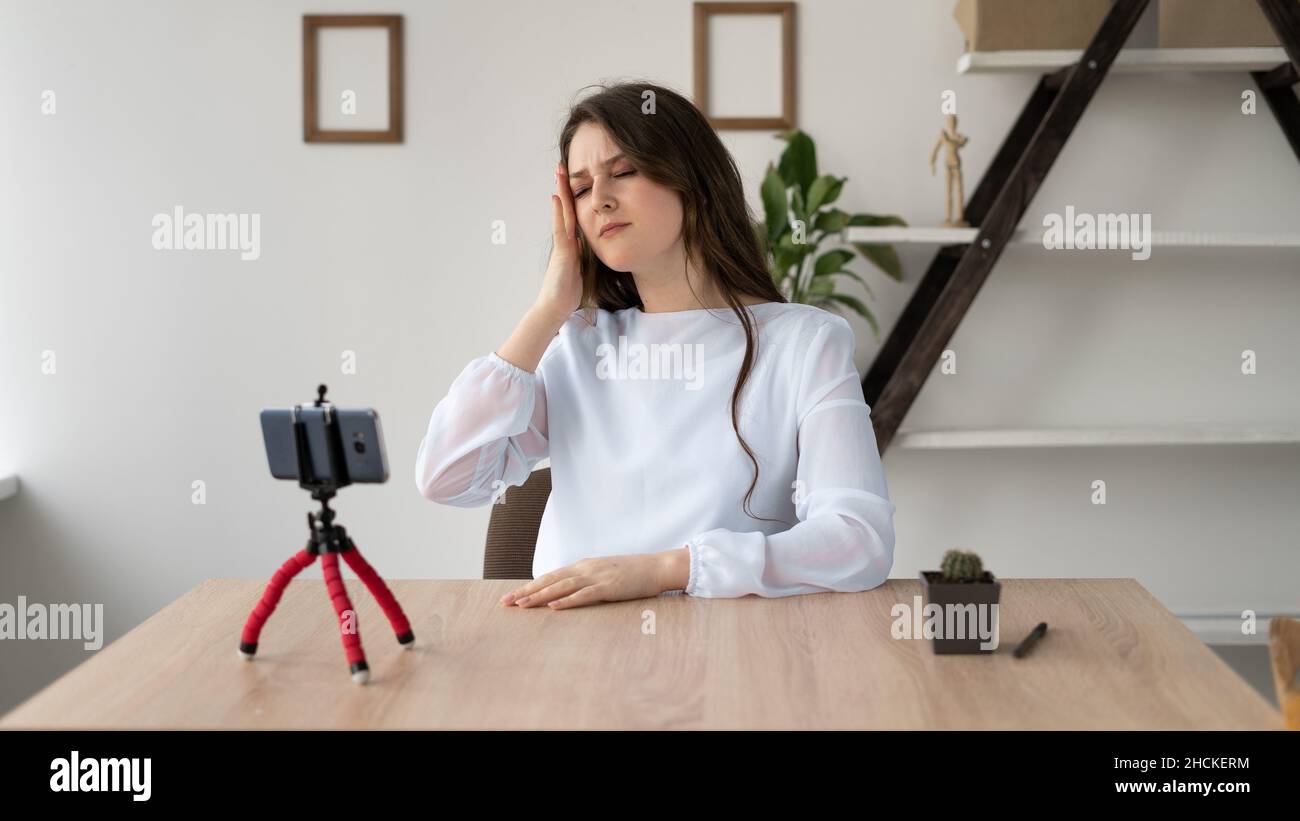 Tired tutor girl with headache sits at a desk at home giving an online ...