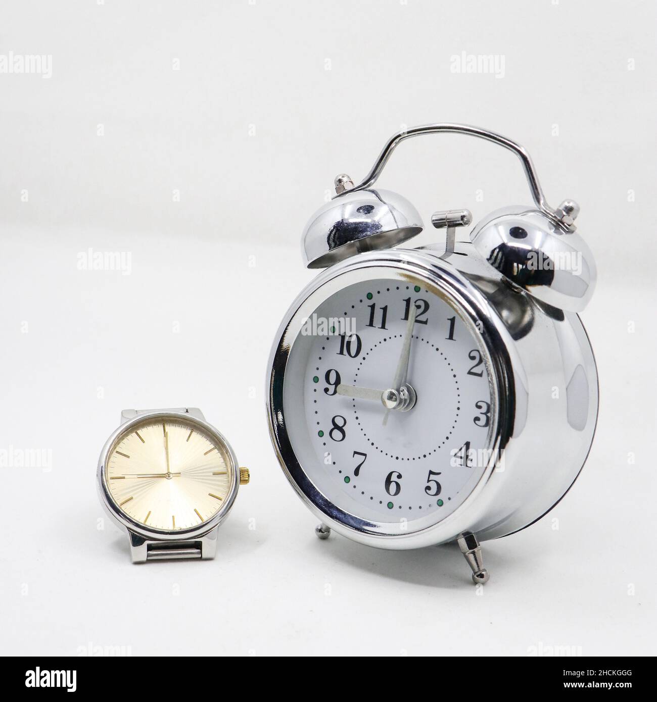 a silver luxury watch and a metallic silver alarm clock for checking ...