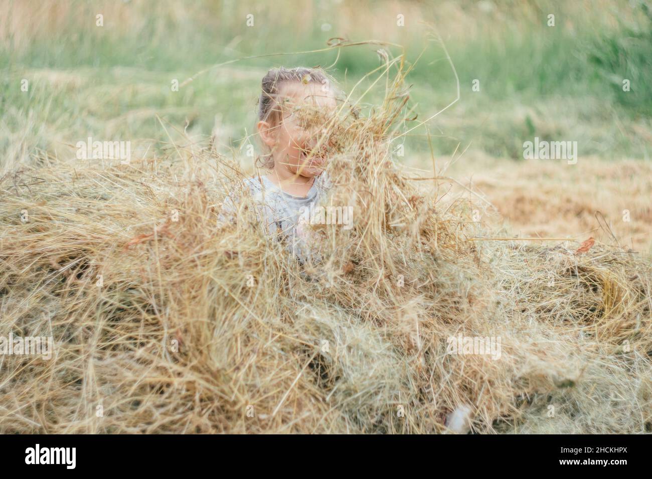 Little girl 3-4 years old jumps and plays in hay stack, throwing it up ...