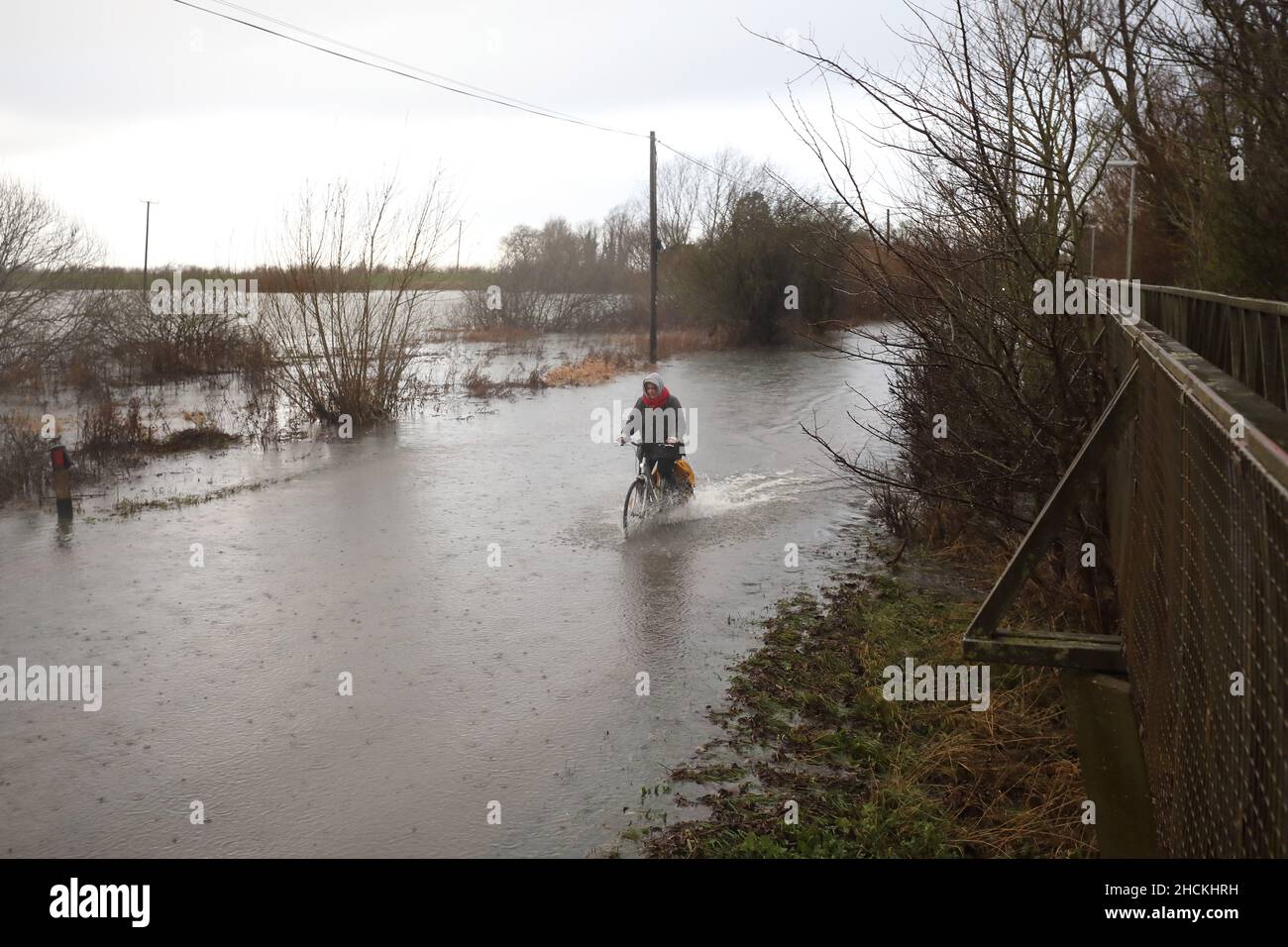 Sutton Gault, UK. 28th Dec, 2021. A person cycles through the flooded ...