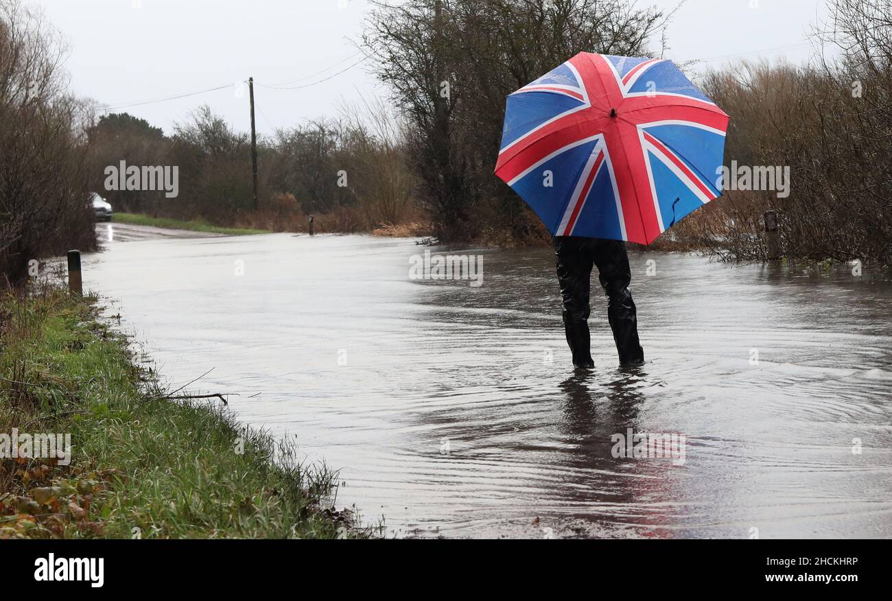 Sutton Gault, UK. 28th Dec, 2021. A person under an umbrella attempts ...
