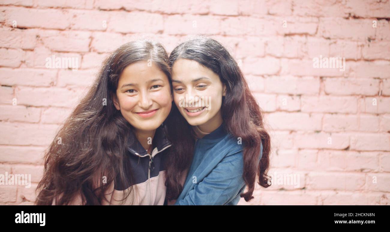 Portrait of two young pretty Indian girls hugging each other against a ...