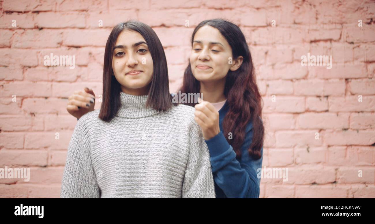 Portrait of two young pretty Indian girls posing against a brick wall ...