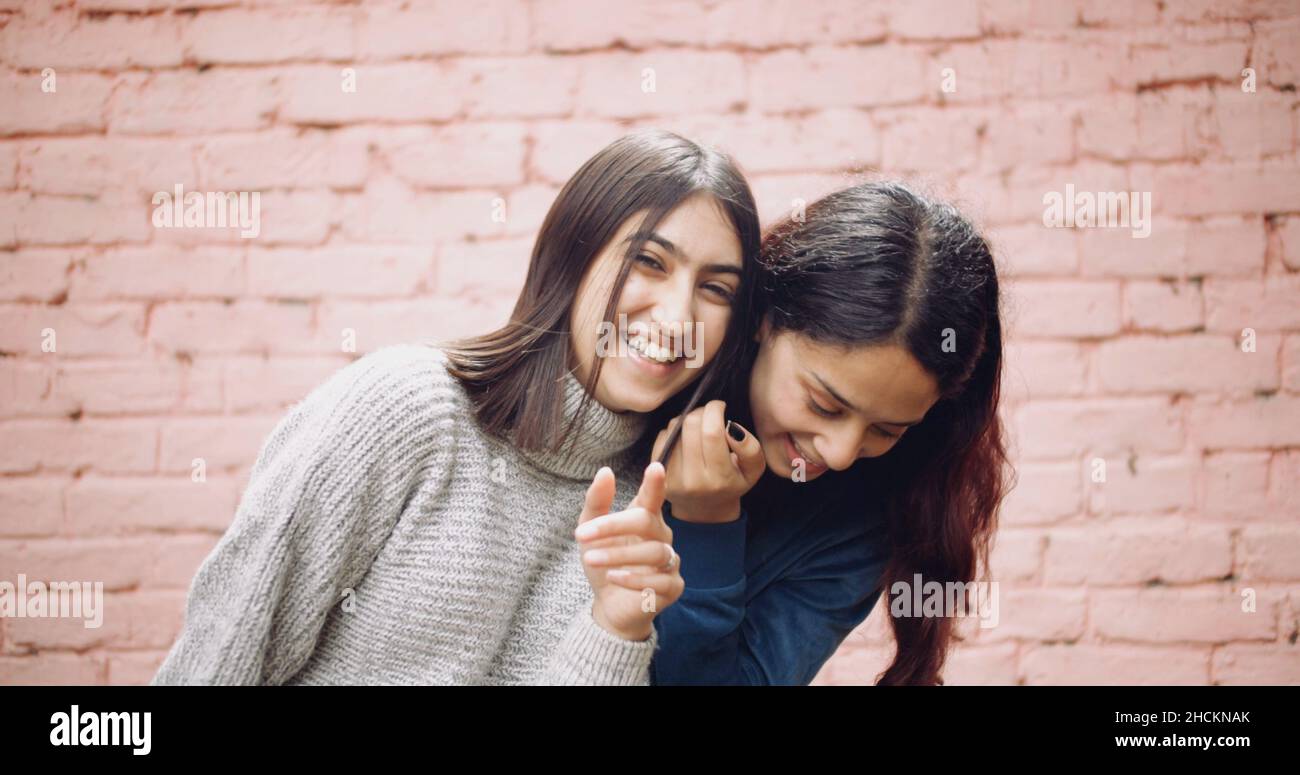 Portrait of two young pretty Indian girls hugging each other against a ...