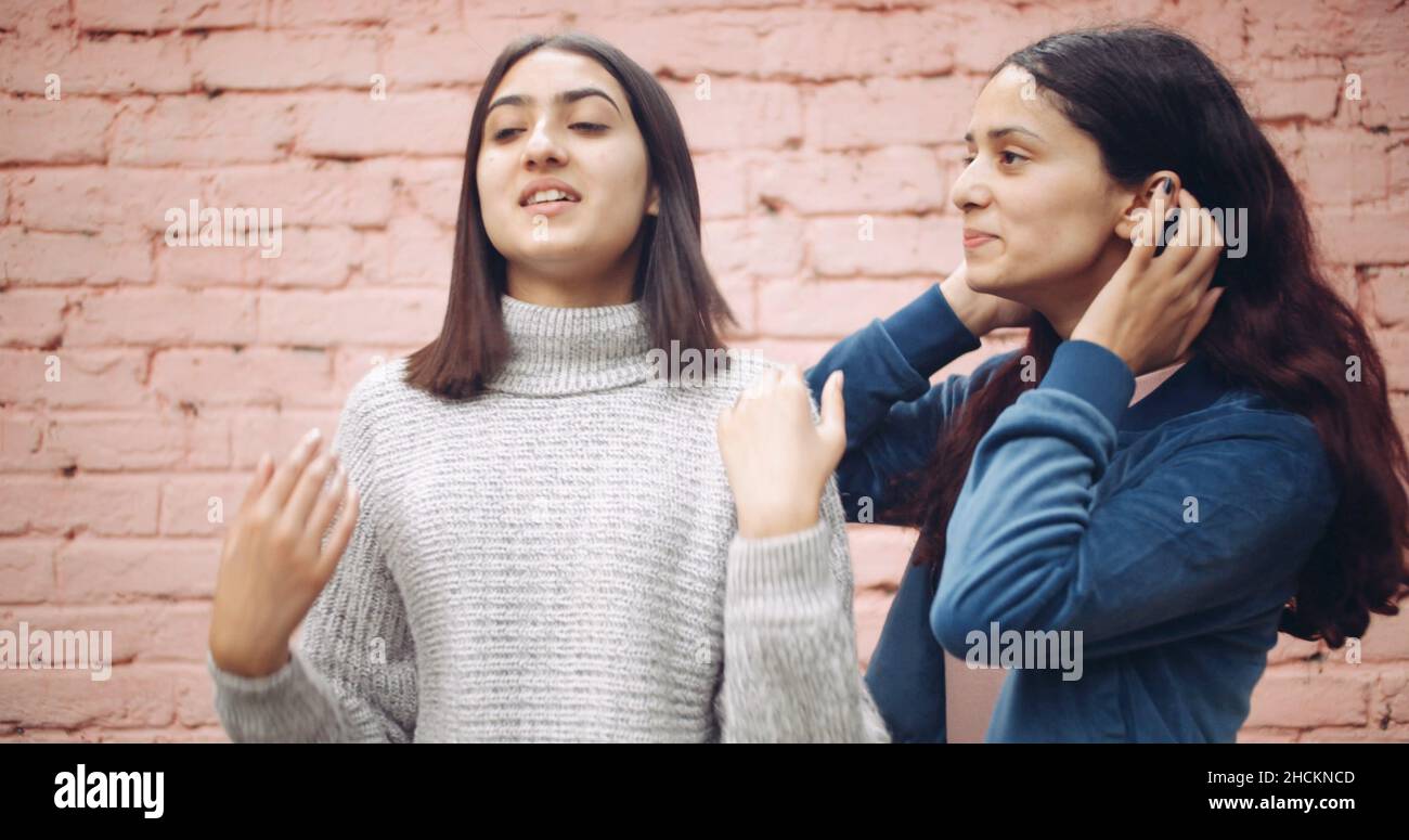 Portrait of two young pretty Indian girls talking against a brick wall ...