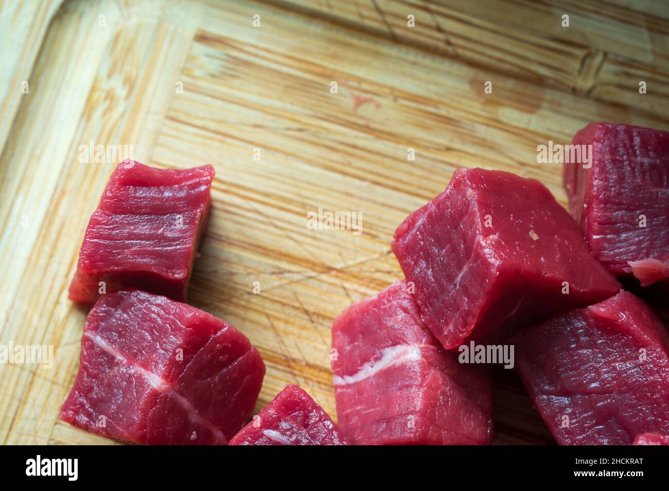 cubes of sliced raw roast beef meat on wooden cutting board closeup ...