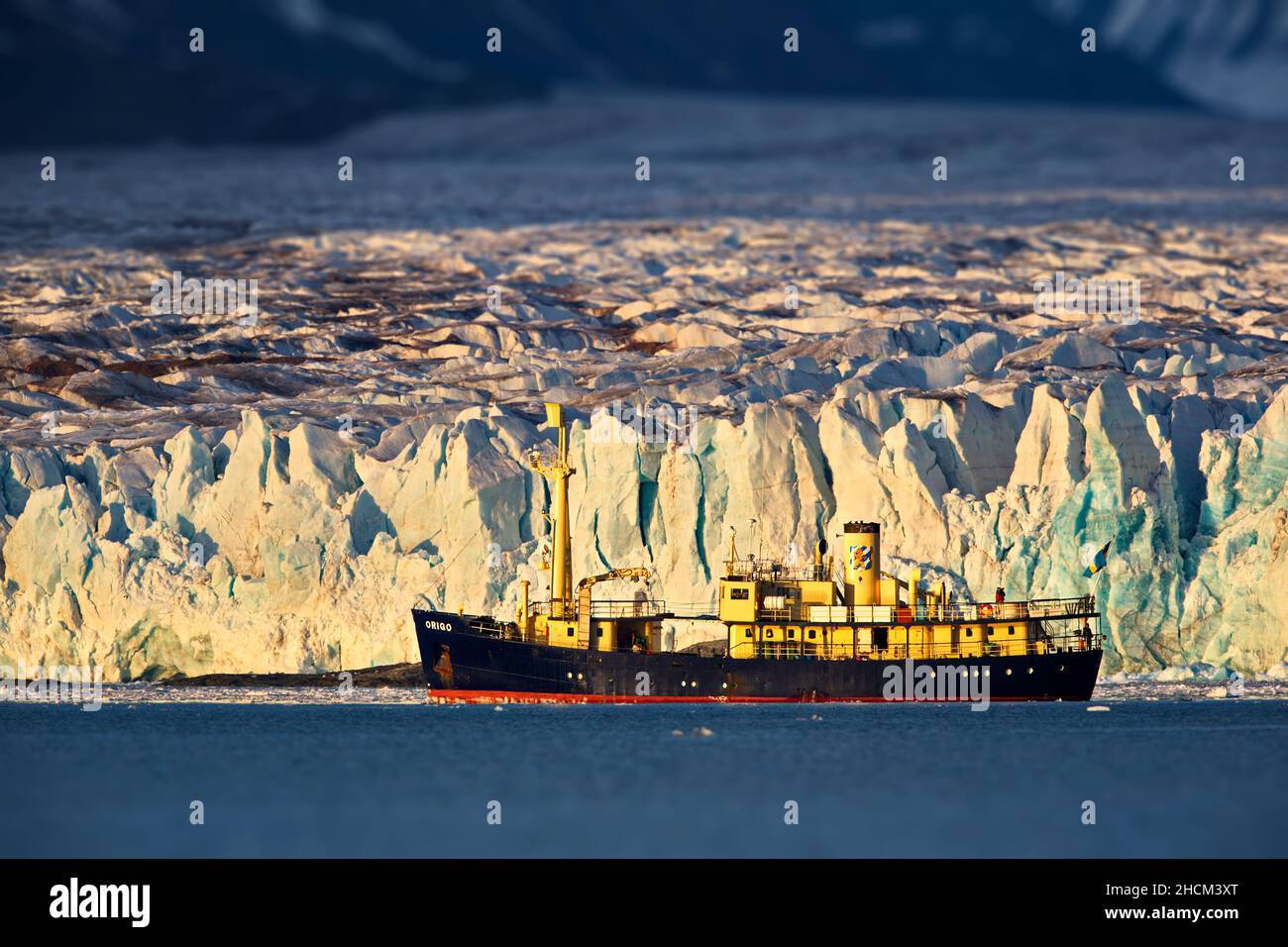 Yellow industrial ship against a massive glacier in Svalbard, Norway ...