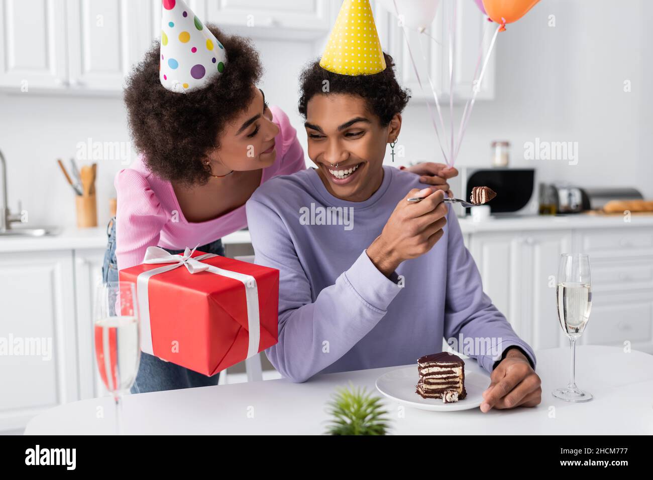 African american woman in party cap holding balloons and present near ...