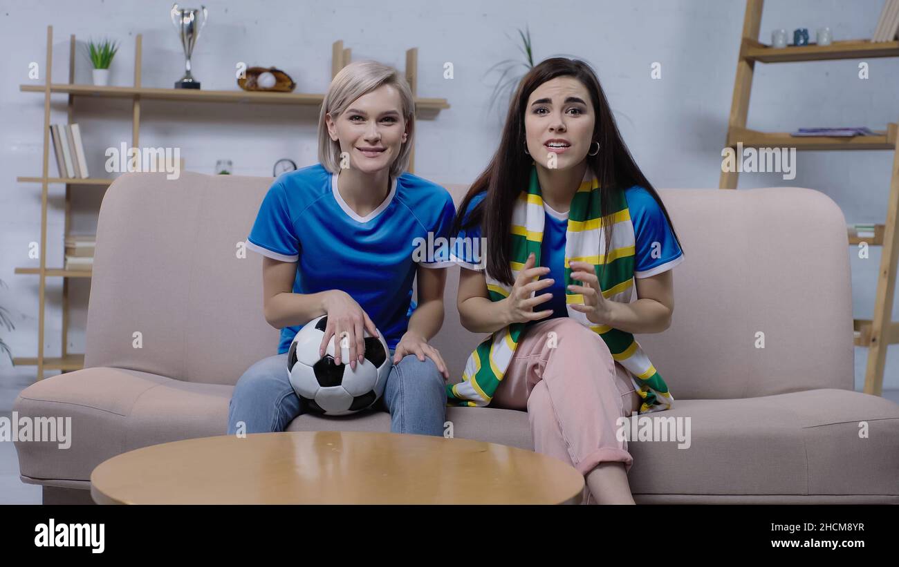 thrilled women watching football championship while sitting on sofa ...