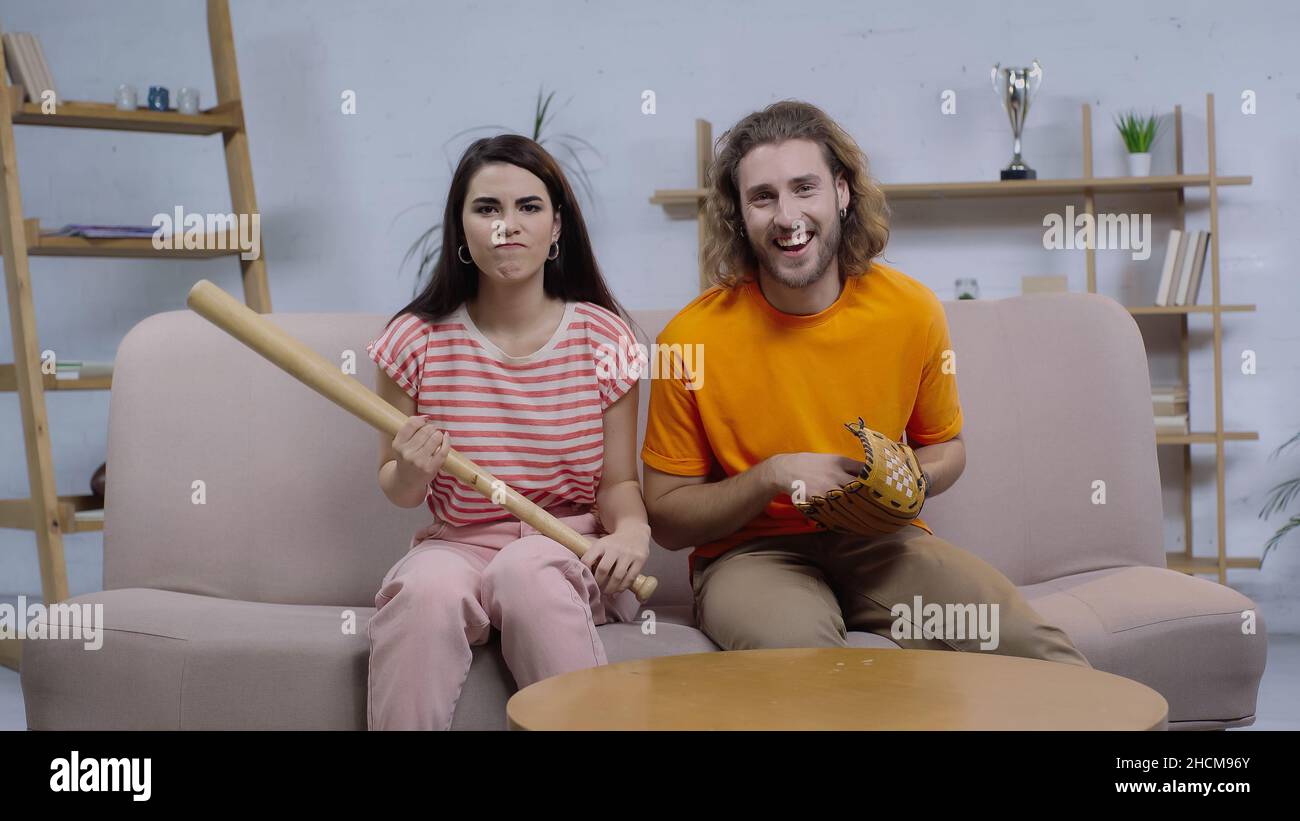 angry woman holding baseball bat near happy man while watching match on ...