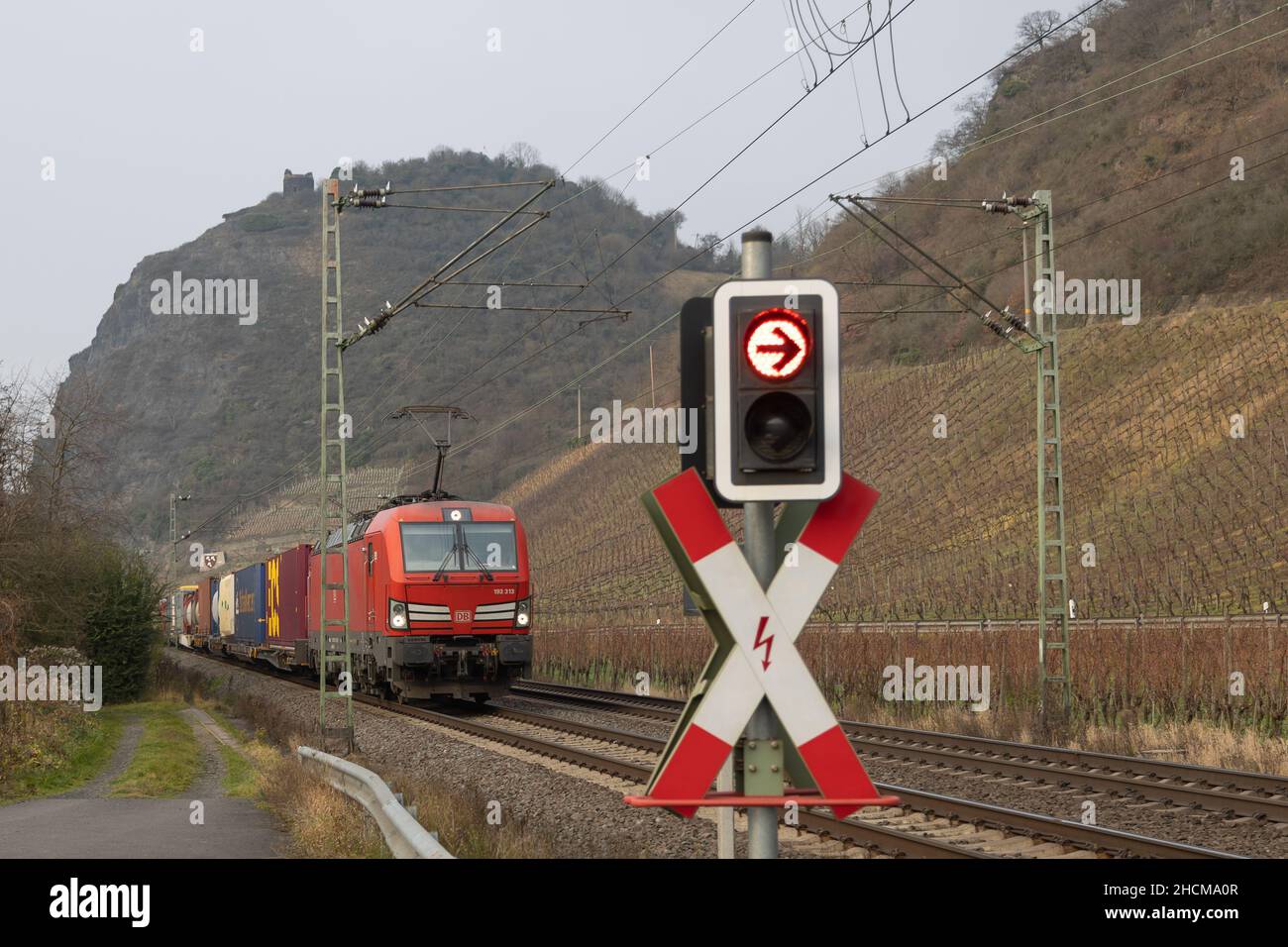 A freight train with a red electric locomotive and a railroad crossing ...