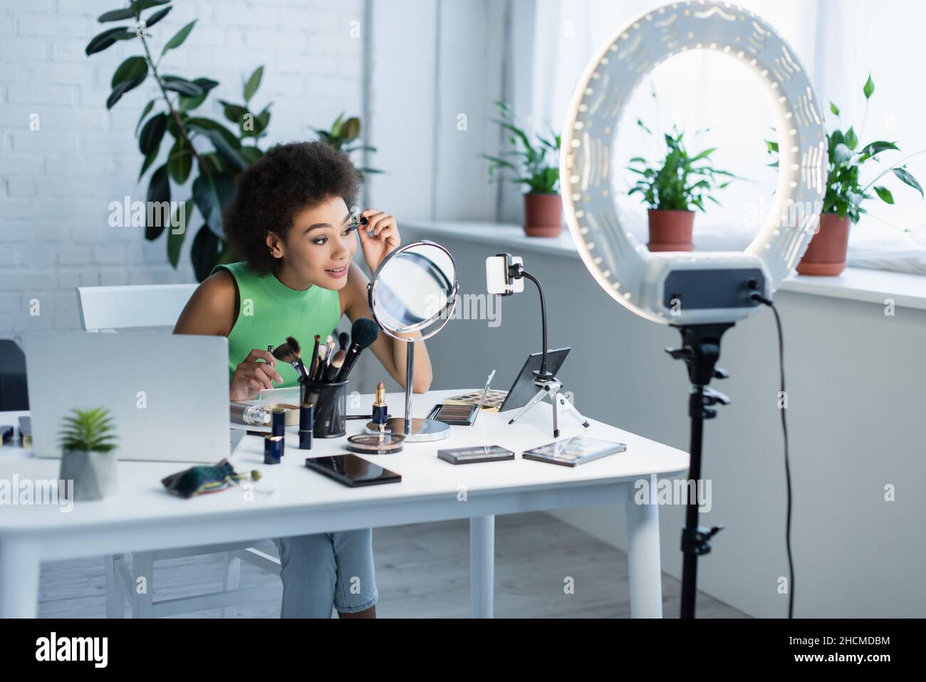 African american blogger applying mascara near gadgets and ring light ...