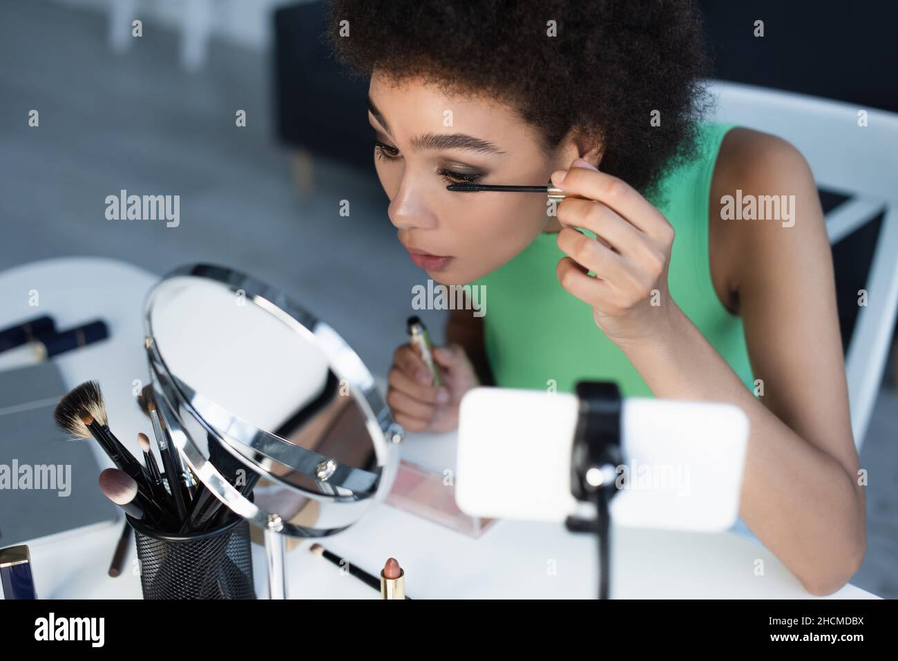 African american blogger applying mascara near cosmetic brushes and ...