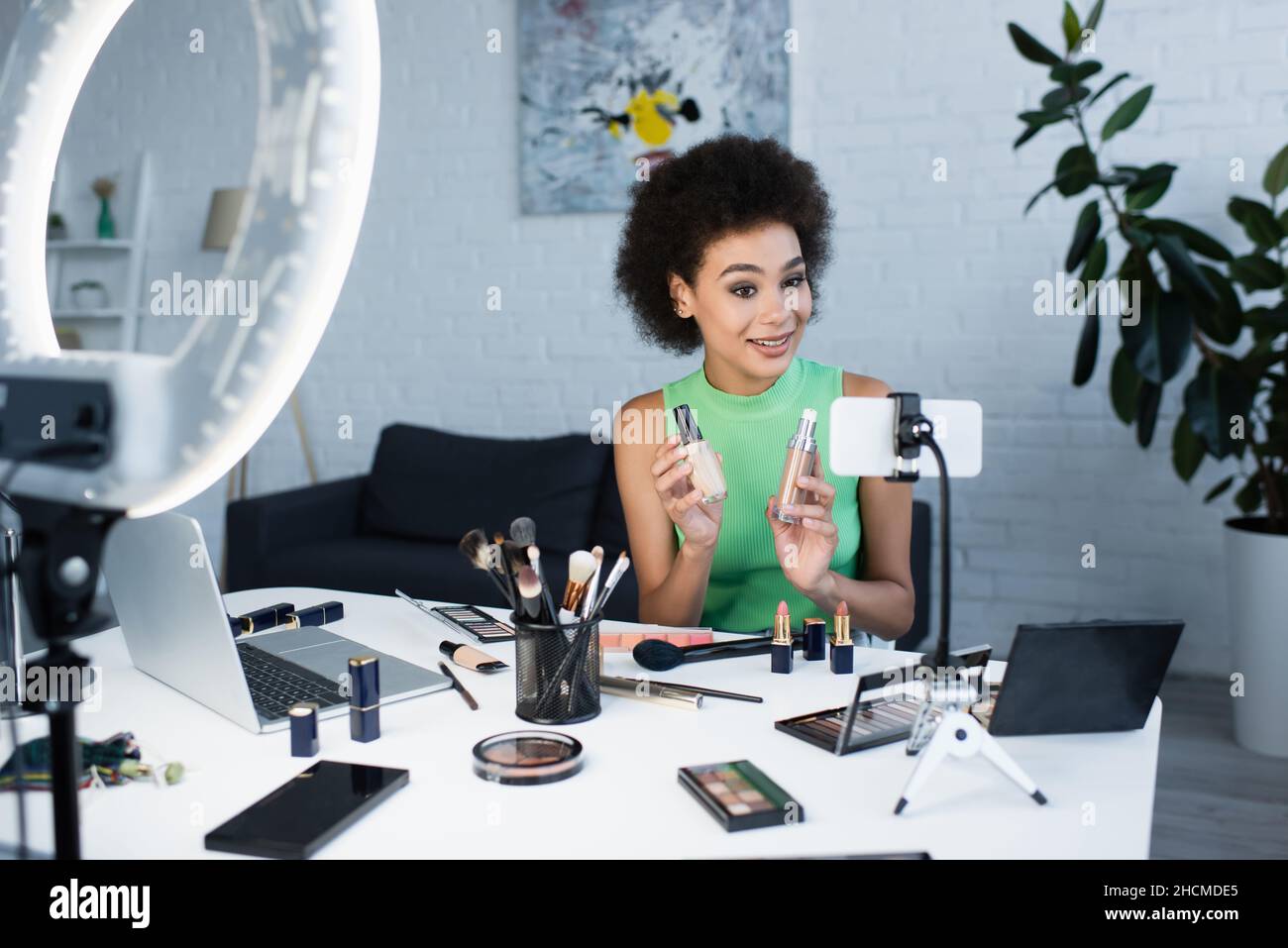 Smiling african american blogger holding face foundations near ...