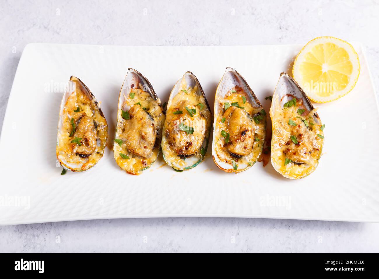 Baked Greenshell mussels in half a shell with cheese, parsley and lemon ...
