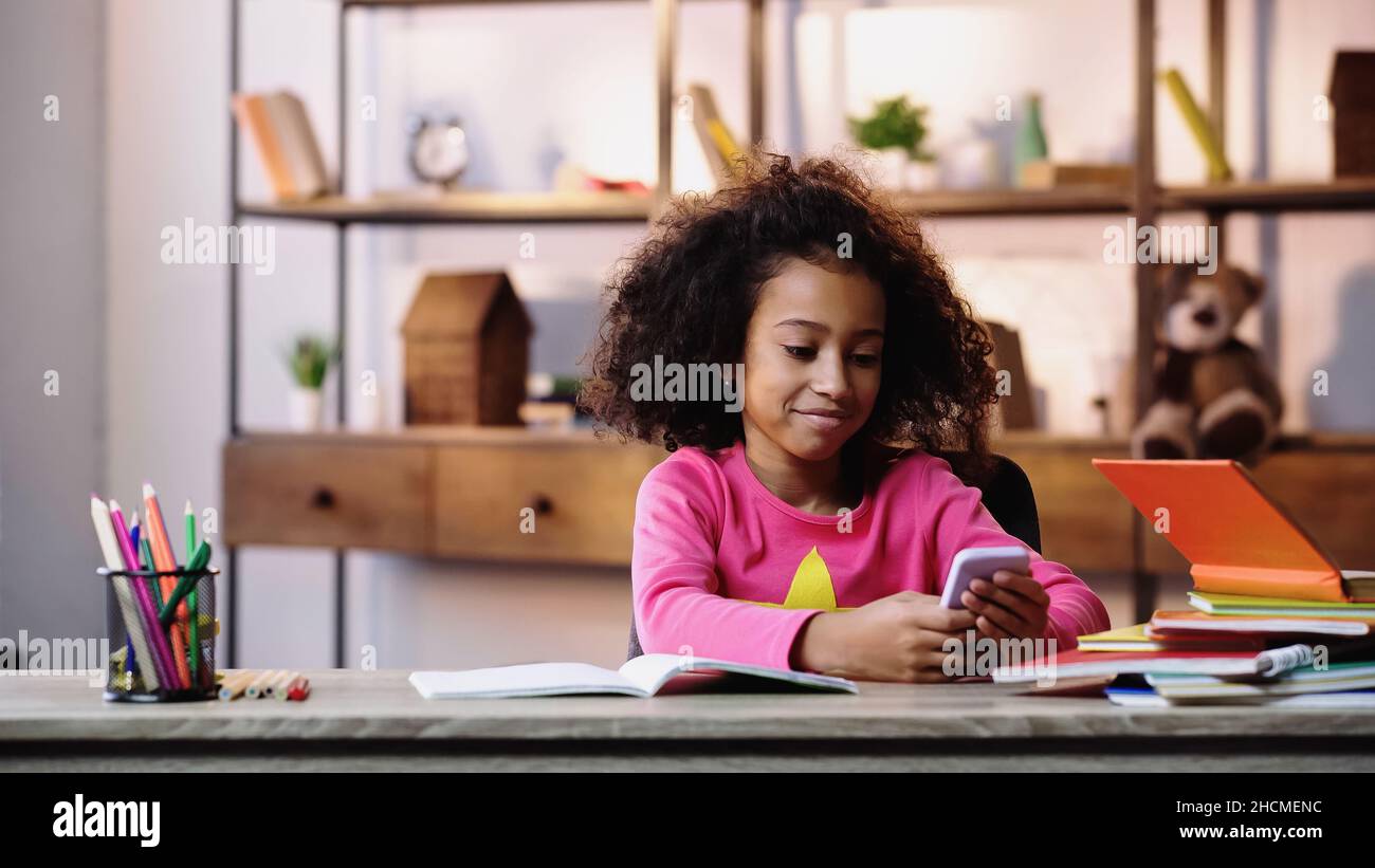 smiling african american child using mobile phone near notebooks Stock ...