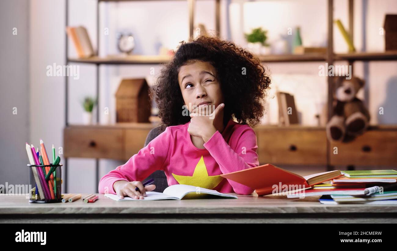 thoughtful african american schoolgirl winking eye and doing homework ...