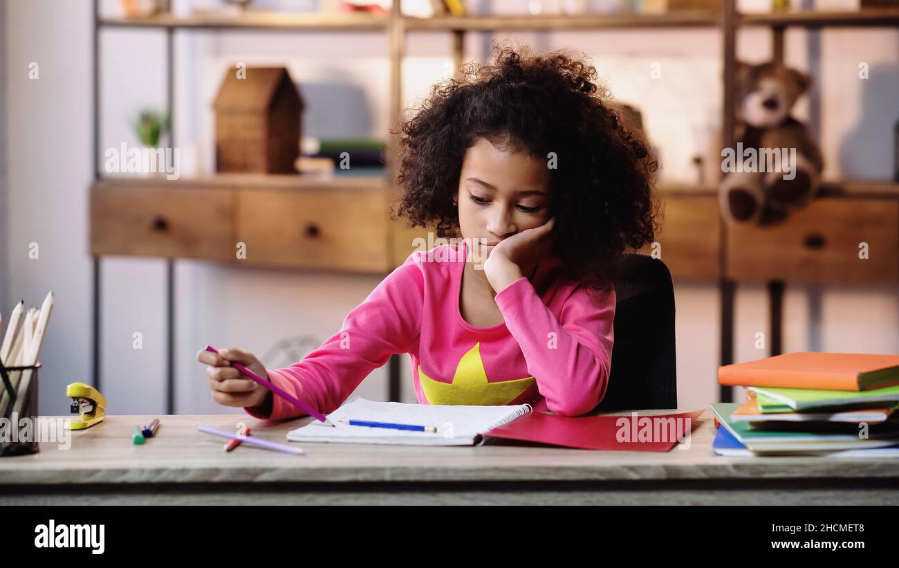 bored african american schoolgirl looking at notebook while doing ...