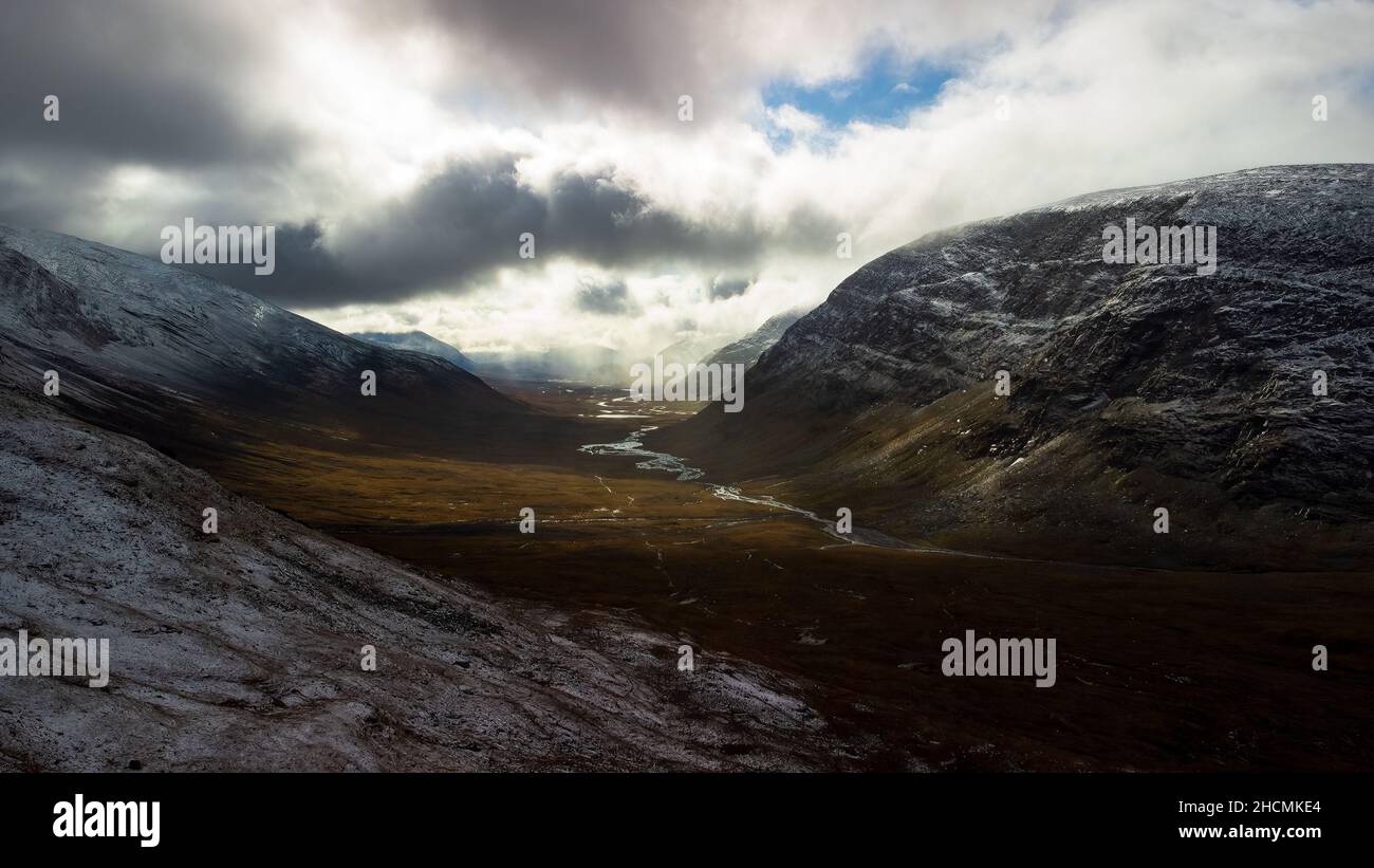 Mountain valley with river between snowy mountains at sunny cloudy day ...