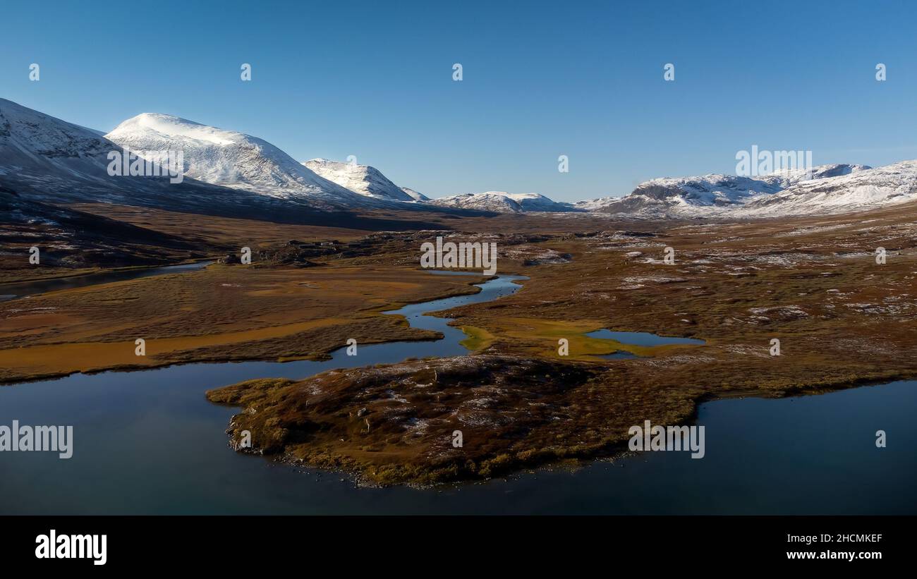 Valley with lake surrounded by snowy peaks at sunny day with no clouds ...