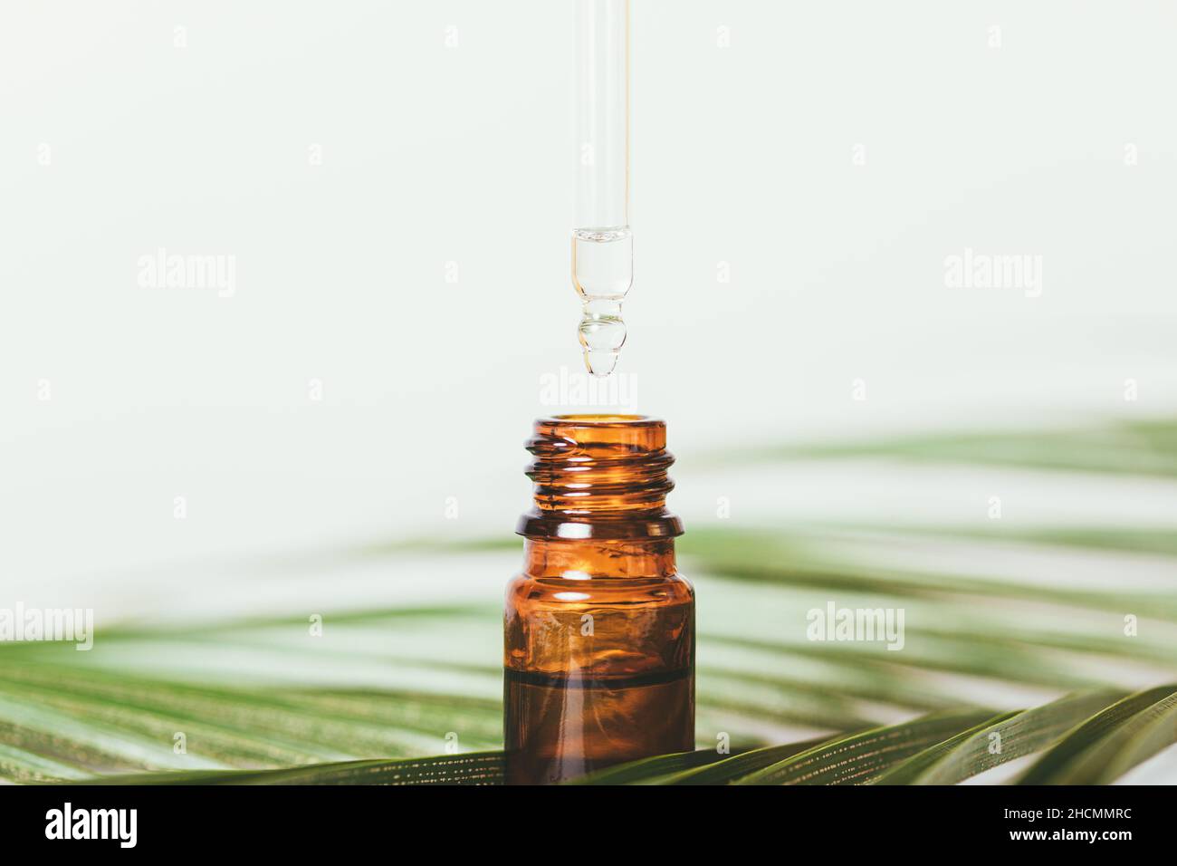 Drop of essential oil drips from pipette into bottle on white ...