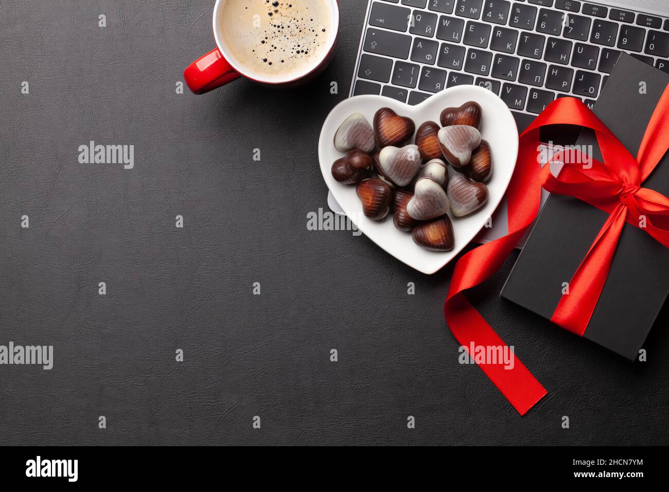 Gift box and chocolate heart sweets over laptop on office desk table ...