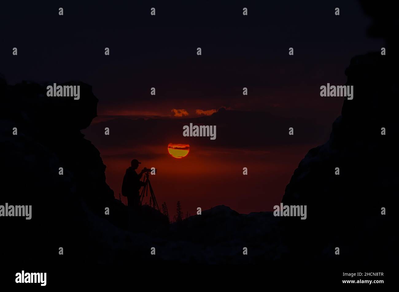 Photographer with a tripod mounted camera showing in silhouette in ...