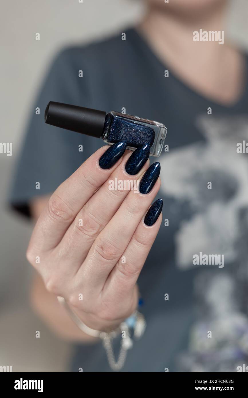 Female hand with long nails and dark blue teal manicure holds a bottle ...