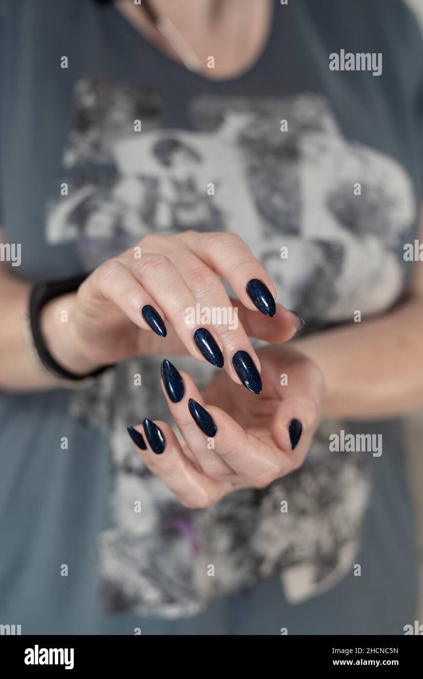 Female hand with long nails and dark blue teal manicure holds a bottle ...