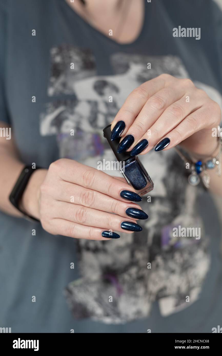 Female hand with long nails and dark blue teal manicure holds a bottle ...