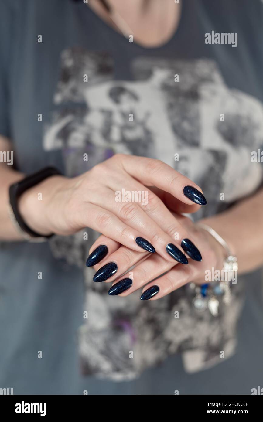 Female hand with long nails and dark blue teal manicure holds a bottle ...