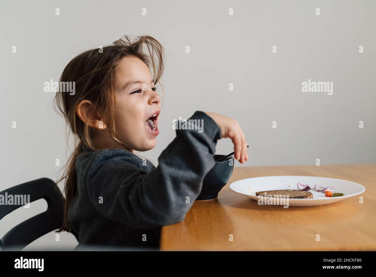 Unhappy child girl eats soup from black bowl with bread and onion ...