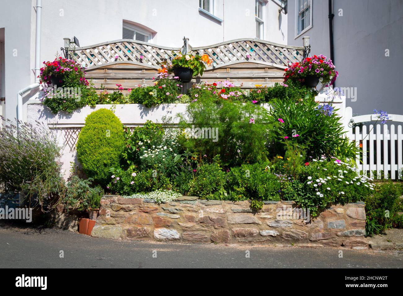 Colourful flowerbed in a raised stone planter against a white fence ...