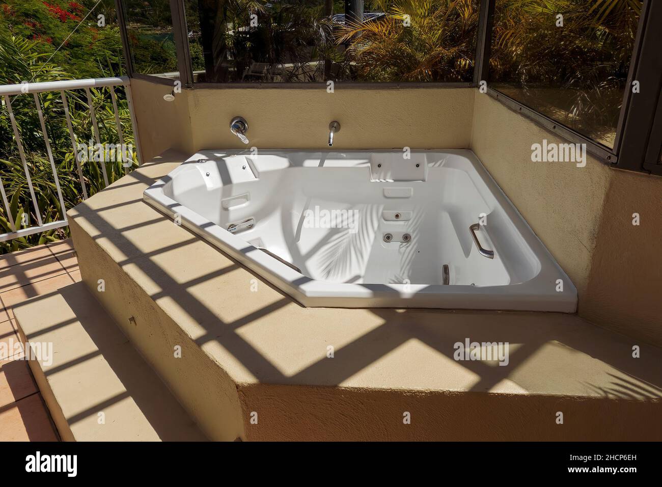 An outdoor spa bath on a deck with shadows from the overhead lattice ...