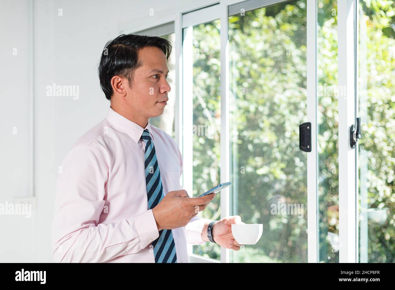 a business man standing by the window using a mobile phone Stock Photo ...