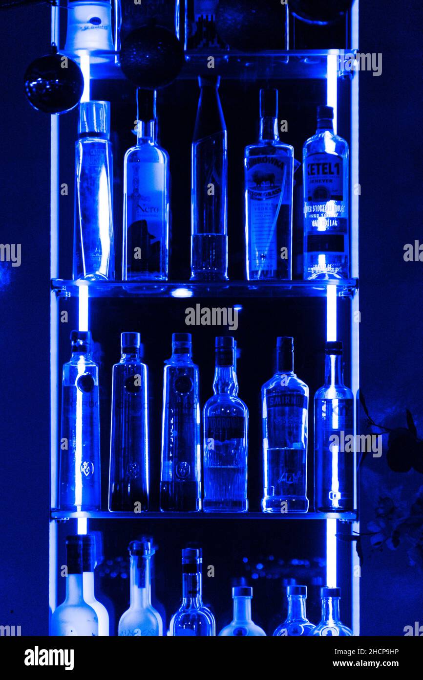 a selection of bottles of alcohol presented on glass shelves with blue ...