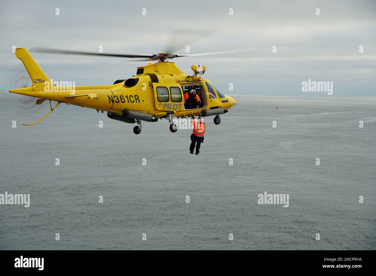Flying yellow helicopter with hanging pilot on the rope ready for ...